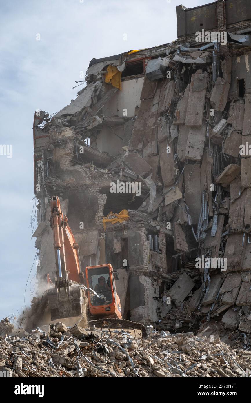 An excavator actively demolishing a large, partially destroyed building ...