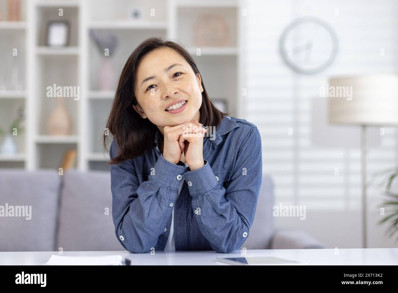 Friendly woman smiling while sitting at a desk in a modern home office ...