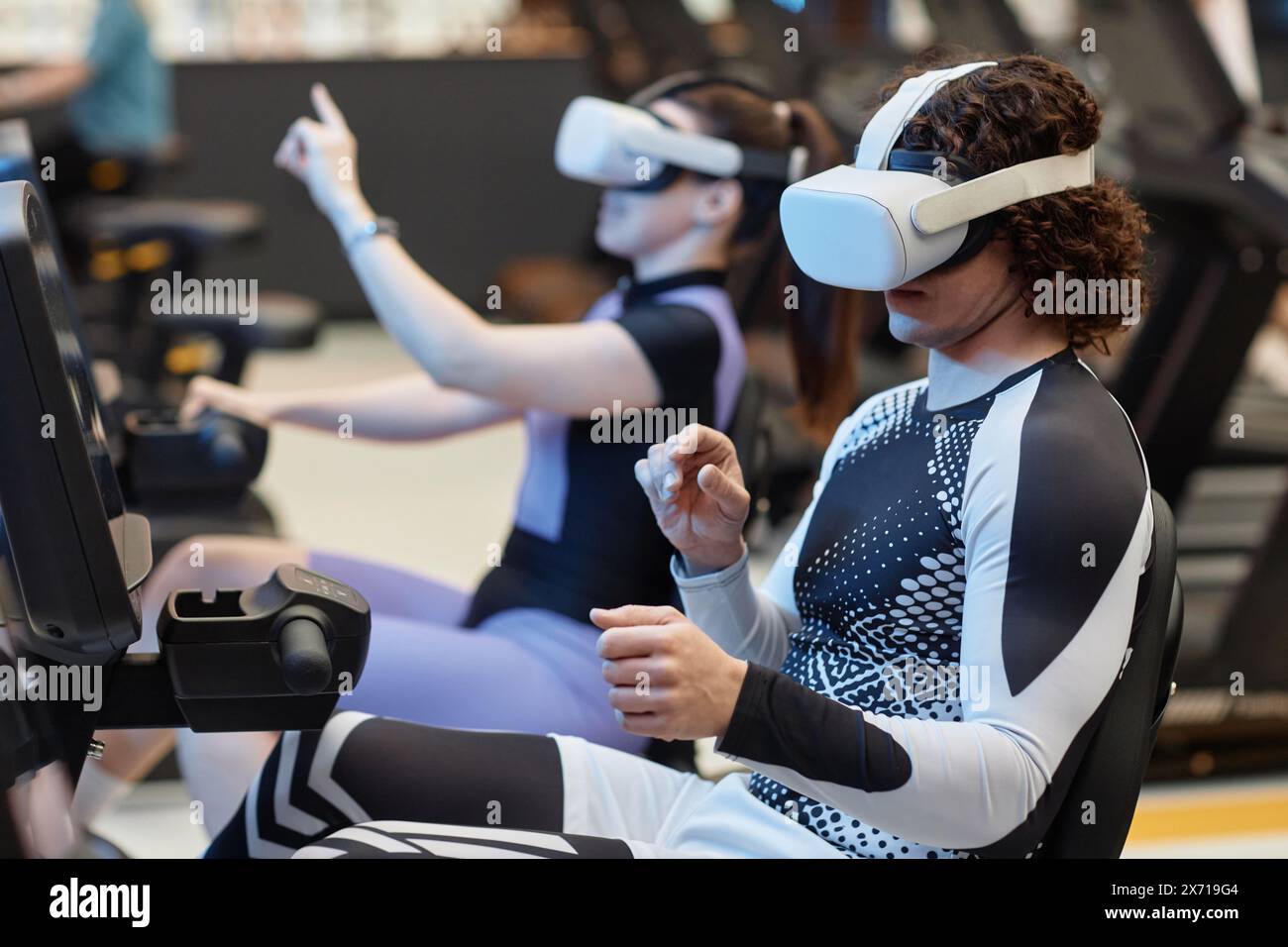Side view portrait of young man on exercise bikes in gym wearing VR ...