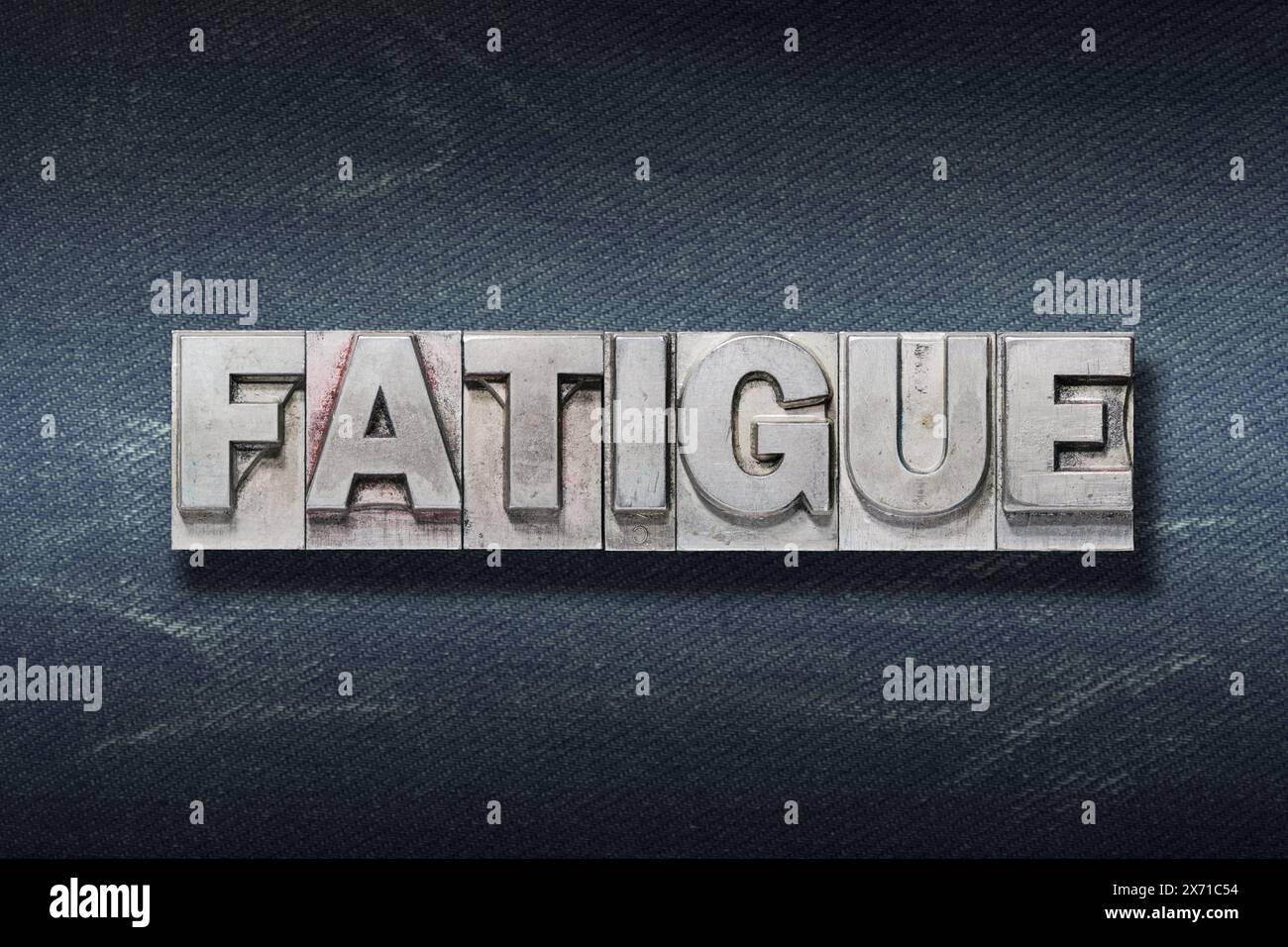 fatigue word made from metallic letterpress on dark jeans background ...