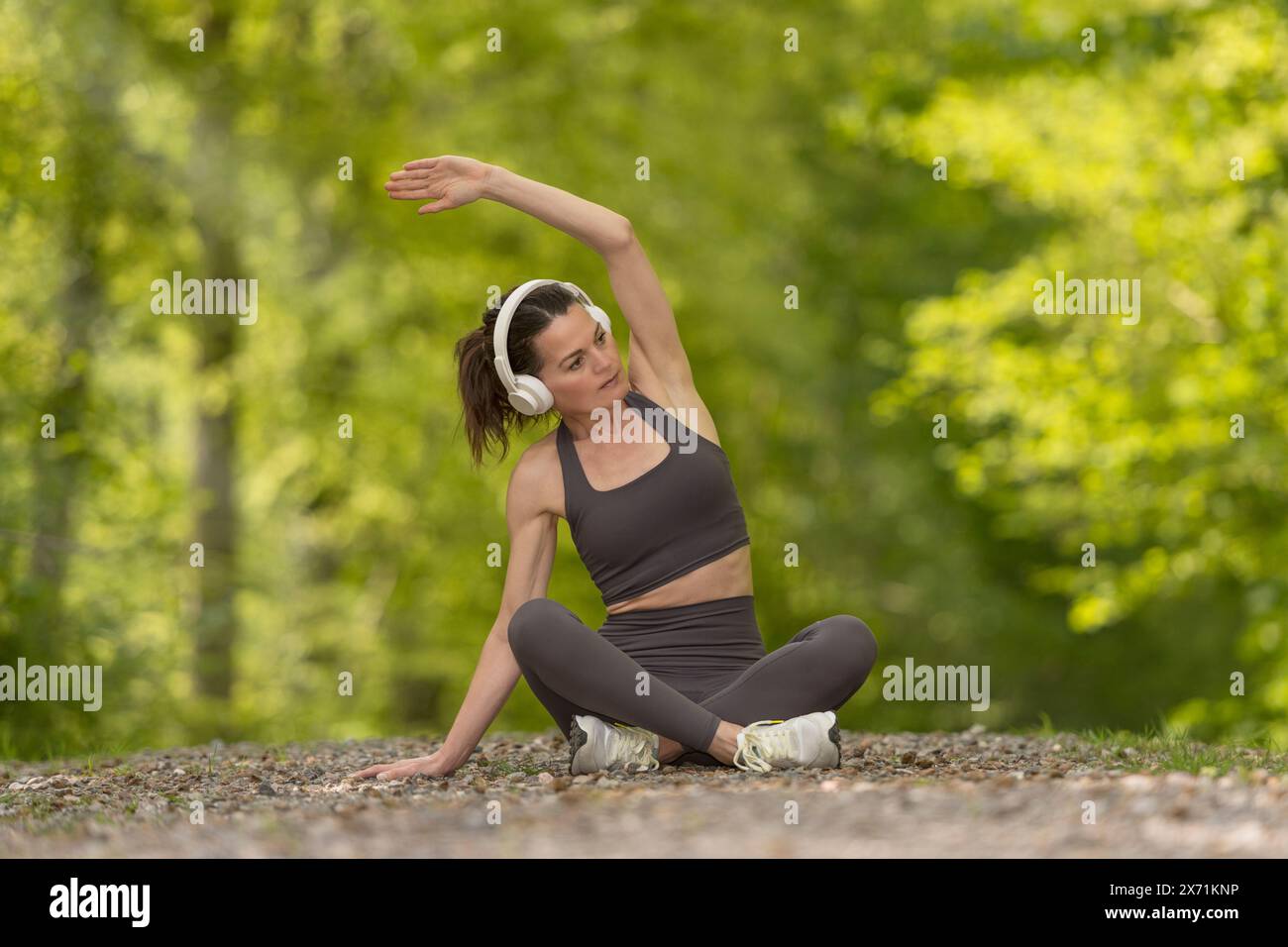 Sporty woman doing stretching exercises outdoors in the park, listening to music with headphones ...