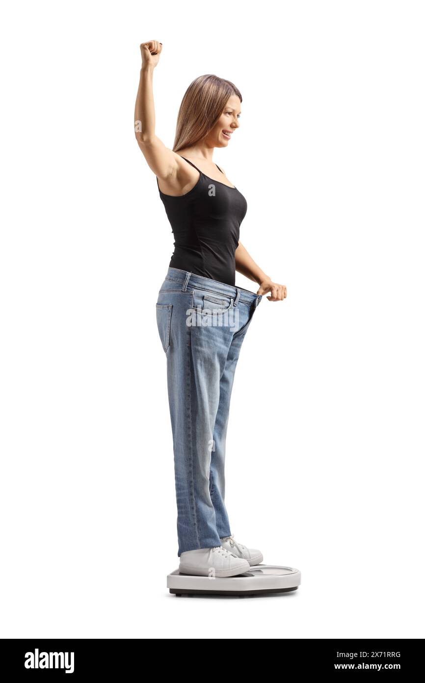 Happy young woman wearing a big size jeans and weighing on a medical ...