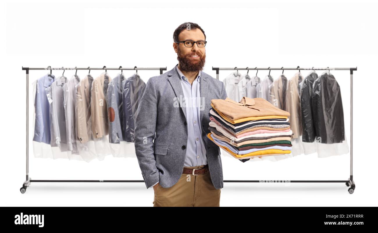 Man holding a pile of folded clothes in front of a rack with clothes on ...