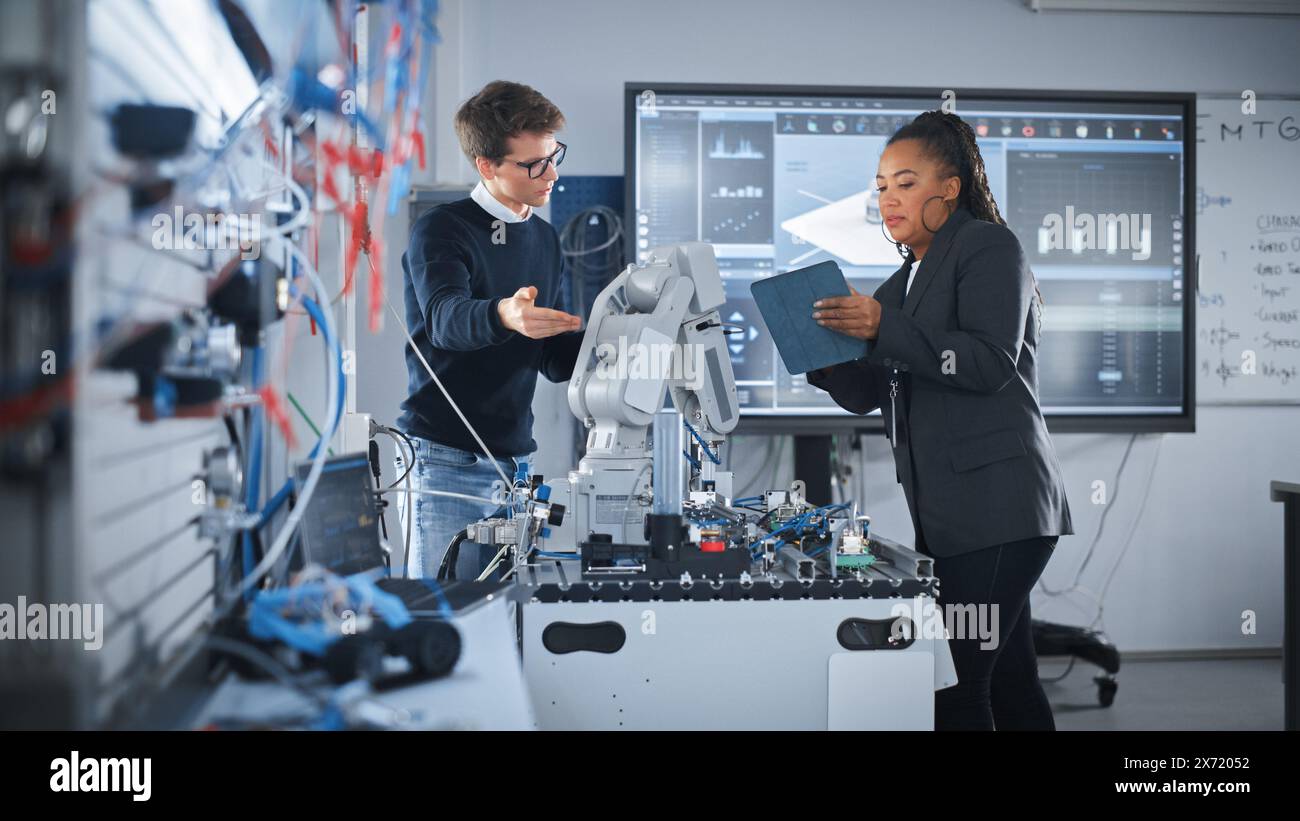 Black Teacher Holding Tablet and Discussing Robot Hand with Caucasian Student During the Lesson ...