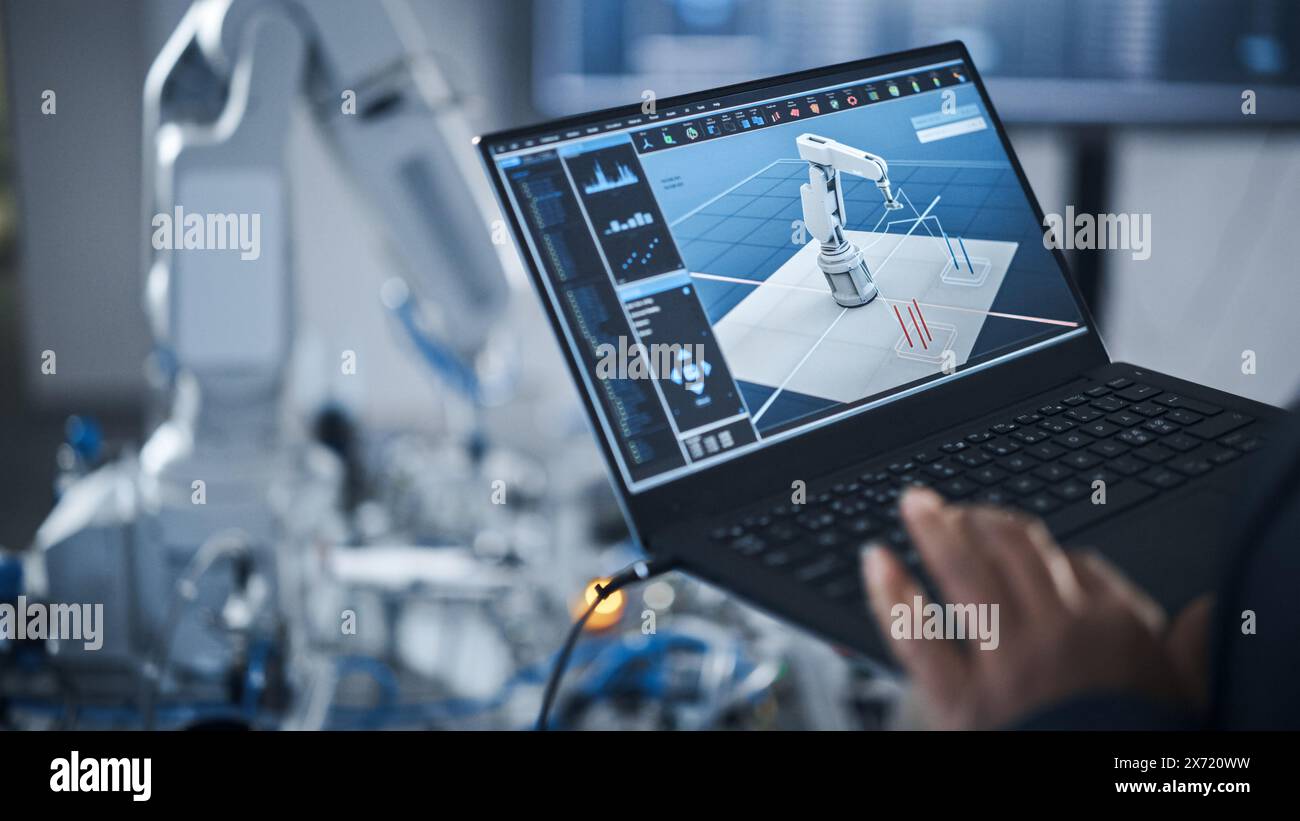 Black Female Engineer Using Laptop For Programming Robotic Arm At The Modern Assembling Factory