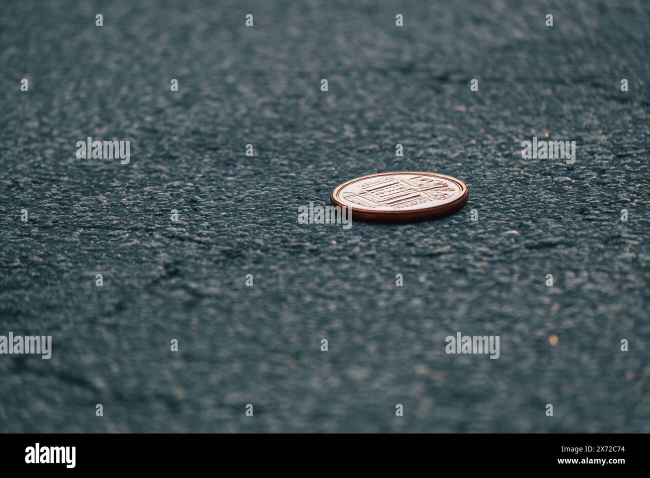 Close-up of a coin lying on an asphalt road. The coin is positioned ...