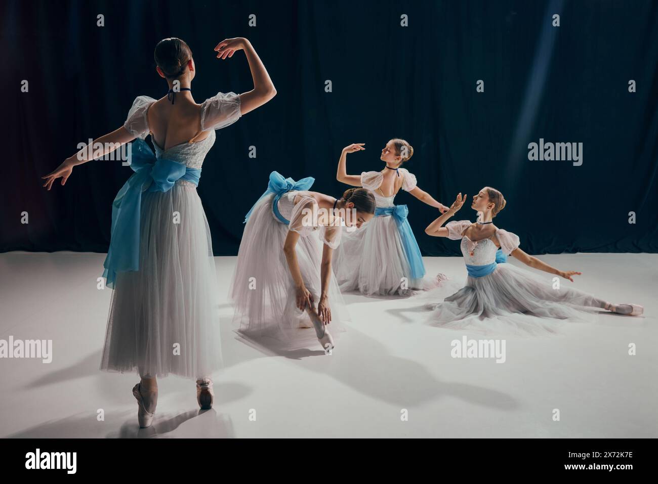 Four ballet dancers in flowing white costumes with blue ribbons ...
