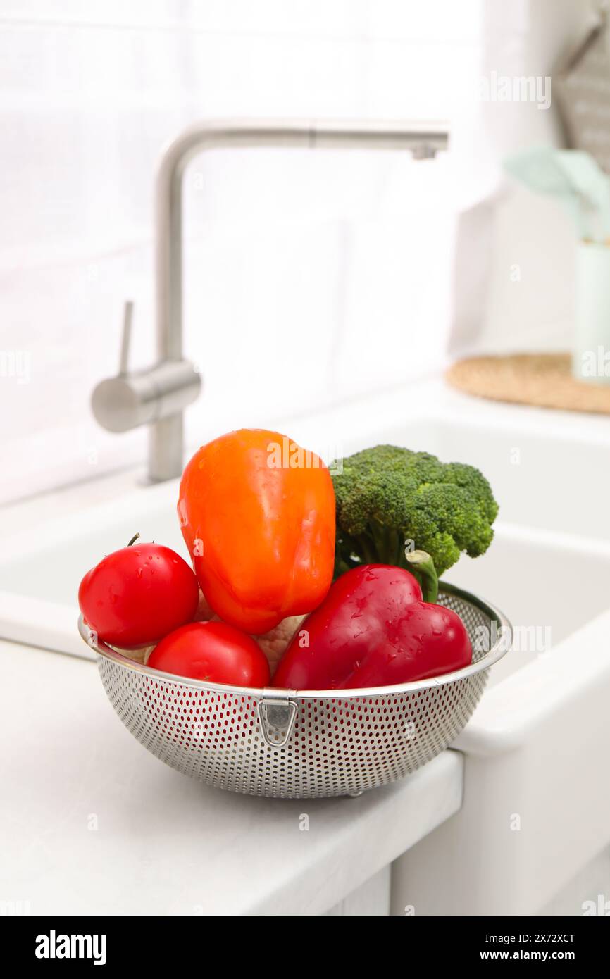 Fresh clean vegetables in colander on countertop near sink Stock Photo ...