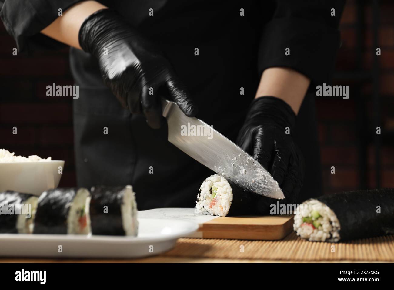 Chef in gloves cutting sushi roll at table, closeup Stock Photo - Alamy