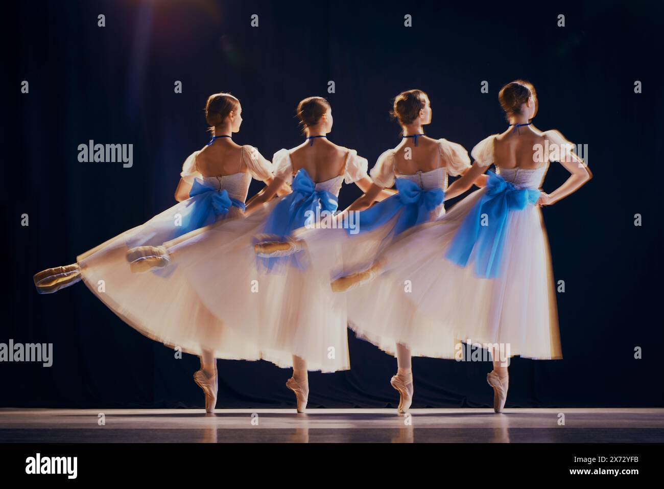 Rear view of young girls, ballet dancers in white tutus with blue bows ...