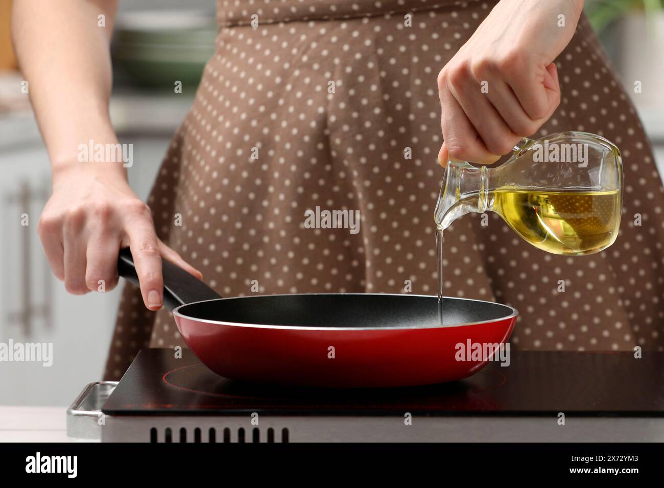 Vegetable fats. Woman pouring cooking oil into frying pan on stove in ...