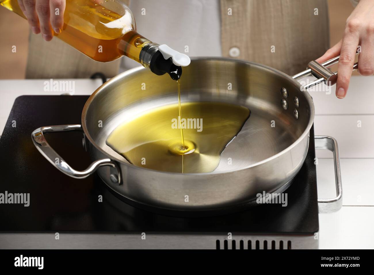Vegetable fats. Woman pouring cooking oil into frying pan on stove ...