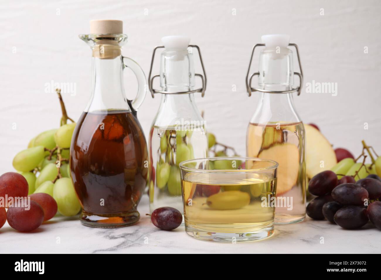 Different types of vinegar and grapes on light marble table, closeup ...