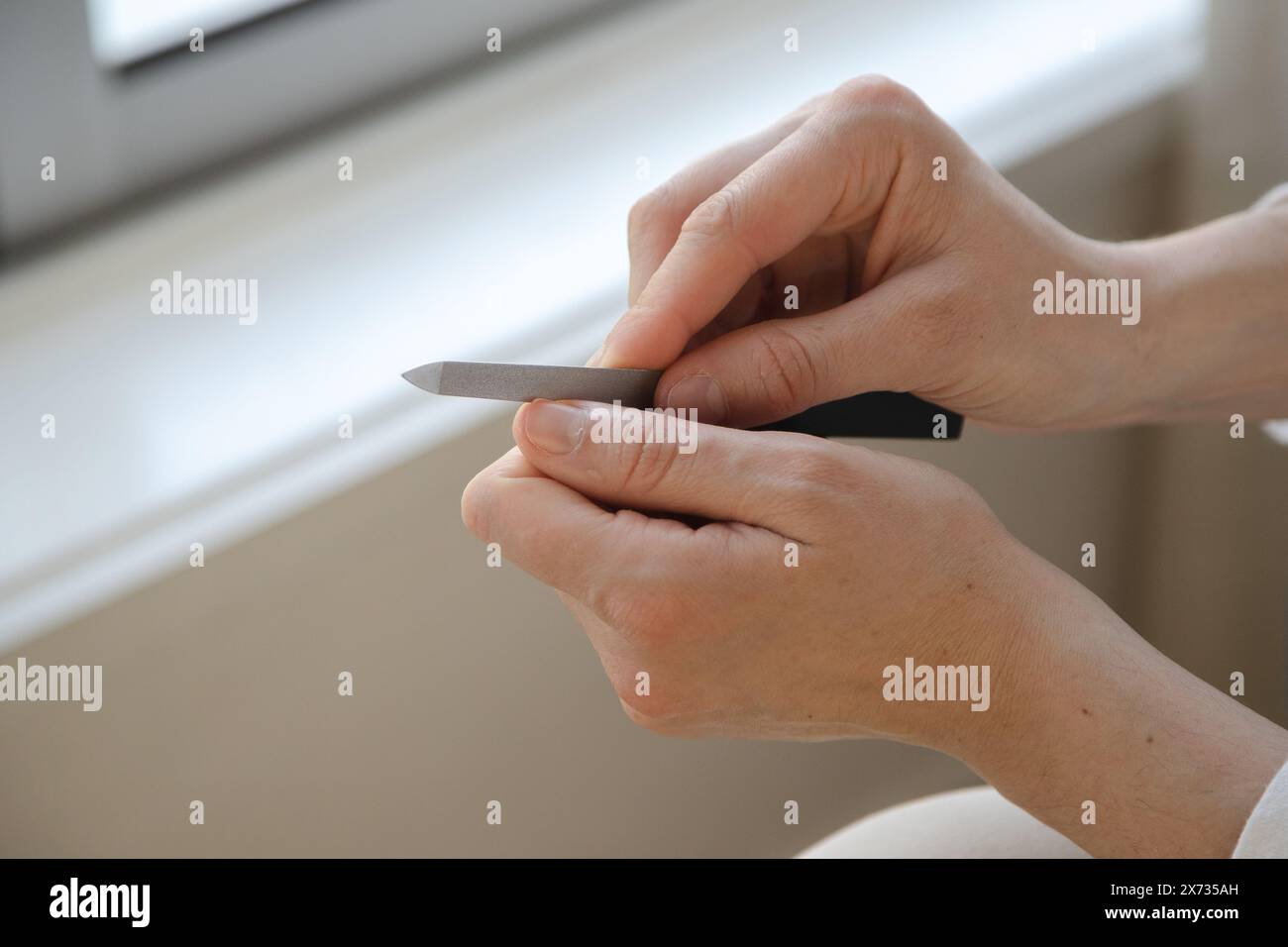 A person carefully filing their nails at home, focusing on self-care ...