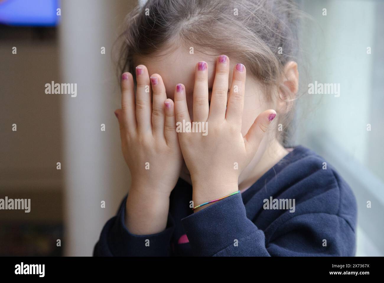 A young girl covers her face with her hands, showing off her freshly ...