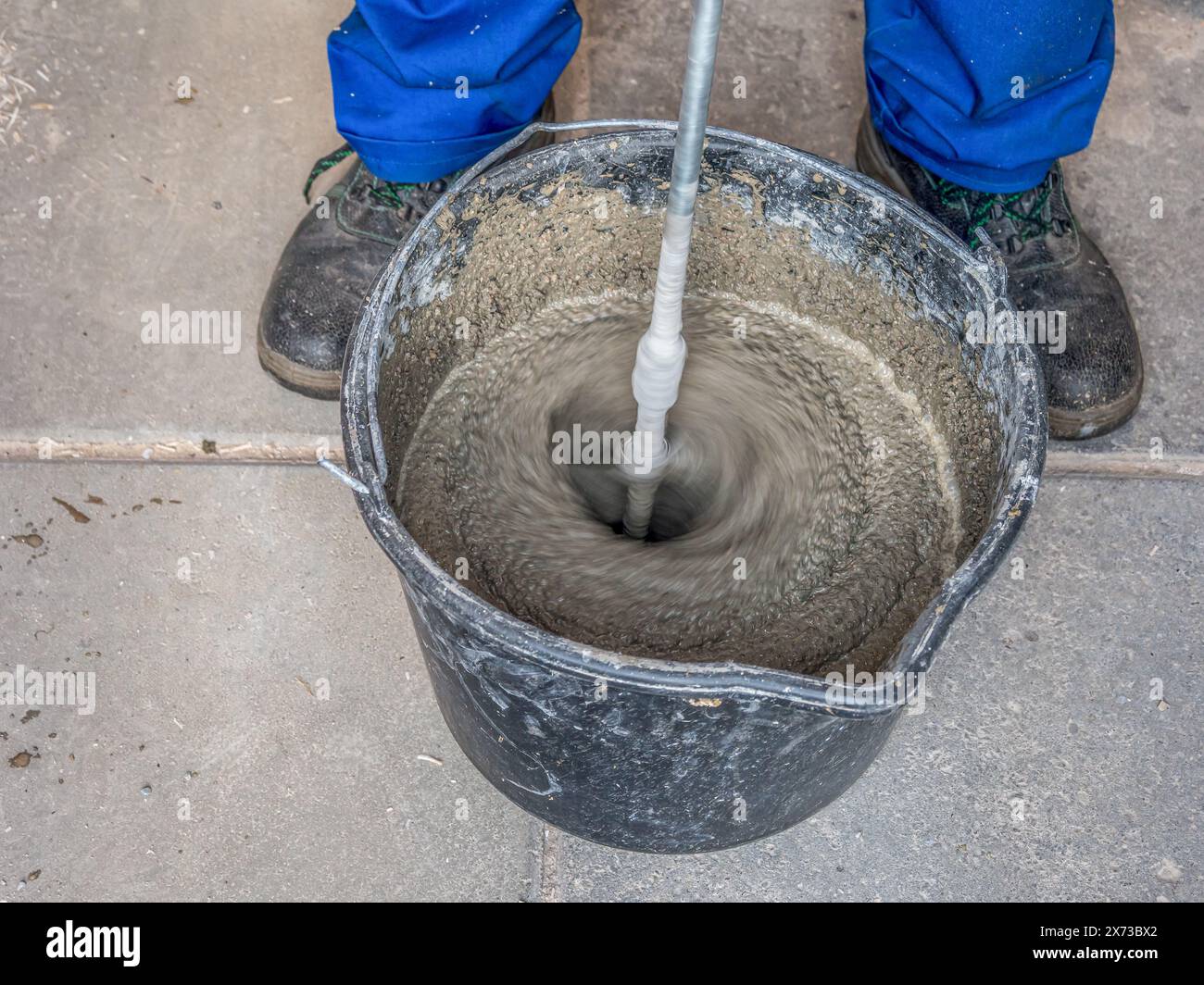 Construction worker mixing mortar in a bucket using handheld concrete ...