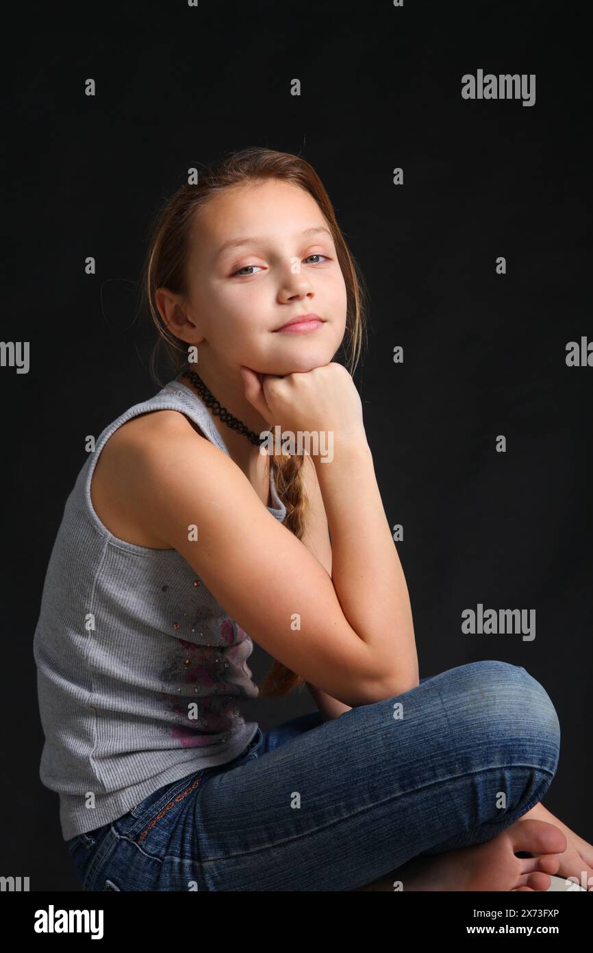 cheerful preteen girl sitting down laughing on black background Stock ...