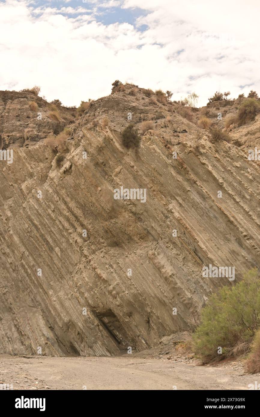 Steep rocky cliff with visible striations and sparse vegetation ...