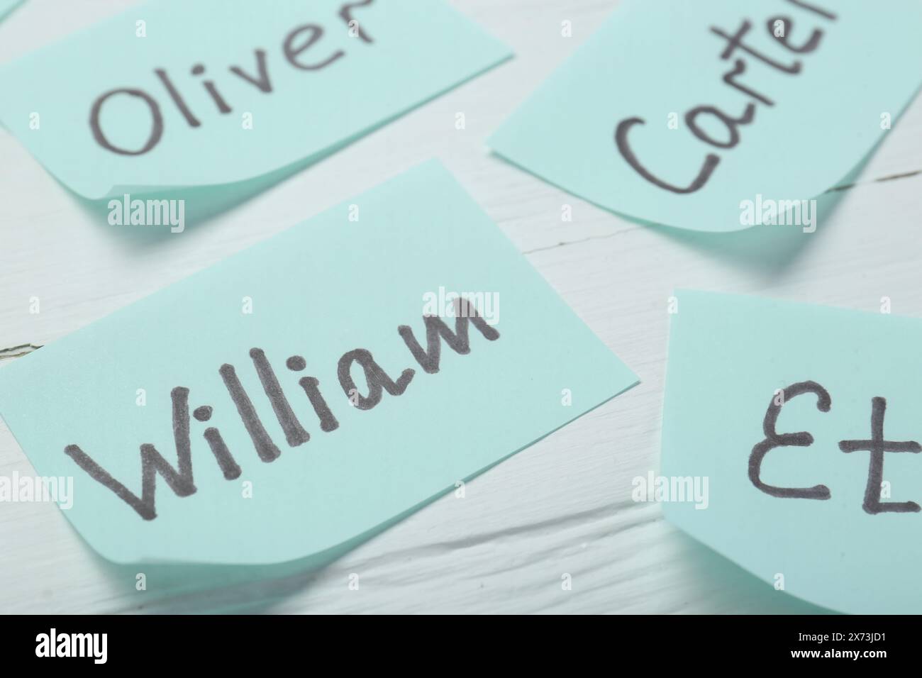 Paper stickers with different names on white wooden table, closeup ...