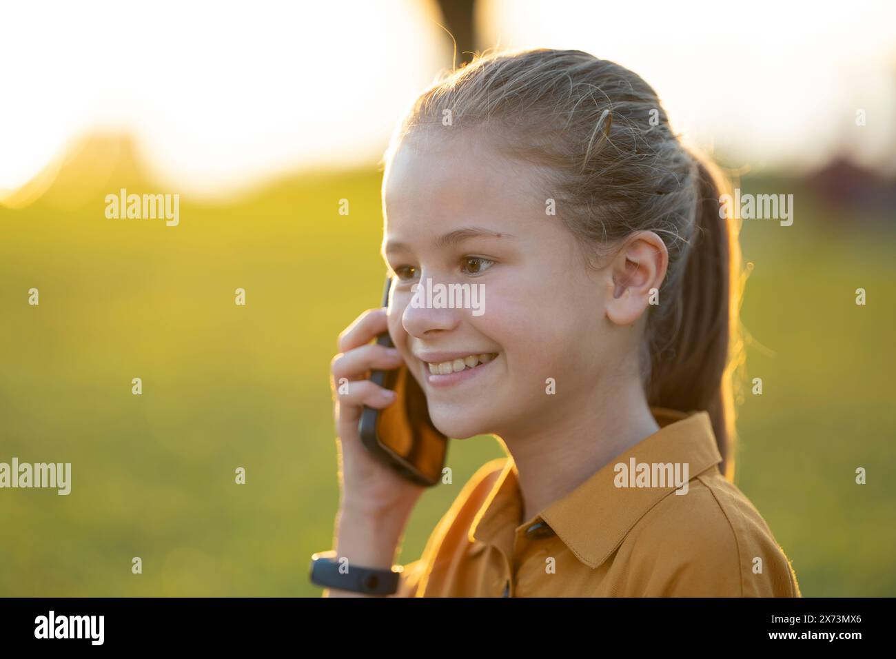 Child girl talking with her friend on cellphone outdoors in summer park ...