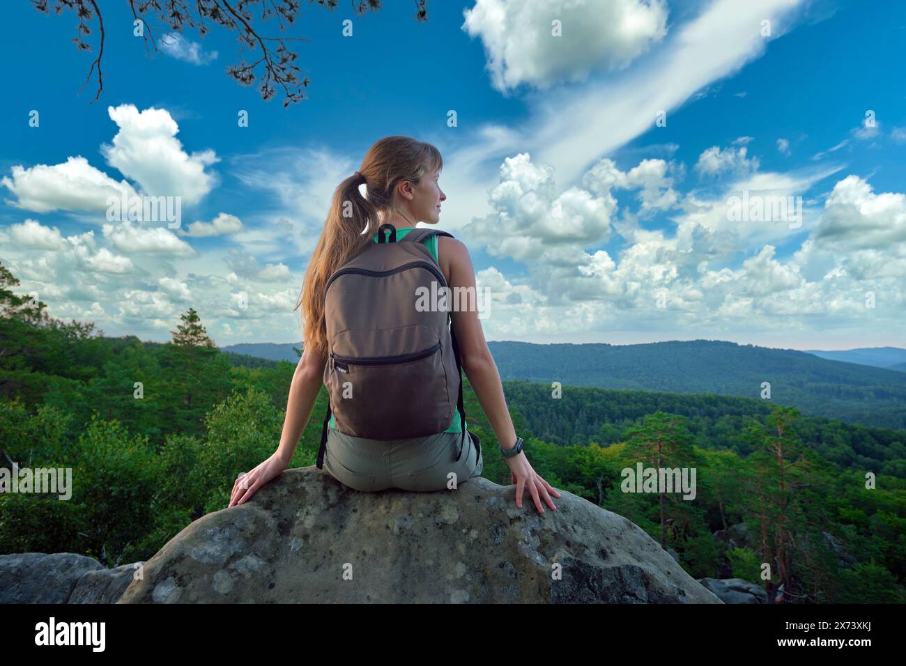 Sportive woman sitting alone taking a break on hillside trail. Female hiker enjoying view of ...