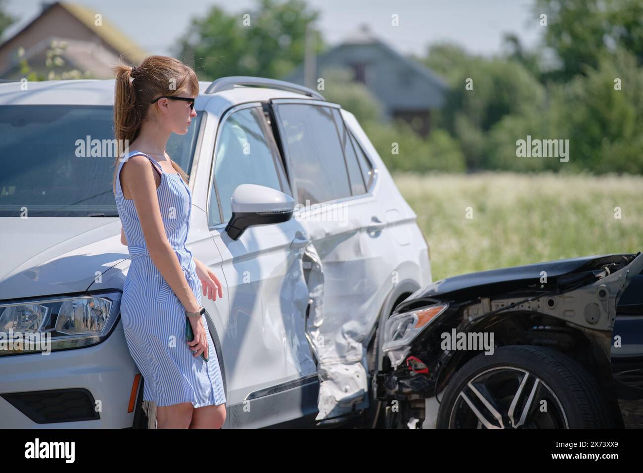 Sad young woman driver standing near her smashed car looking shocked on ...