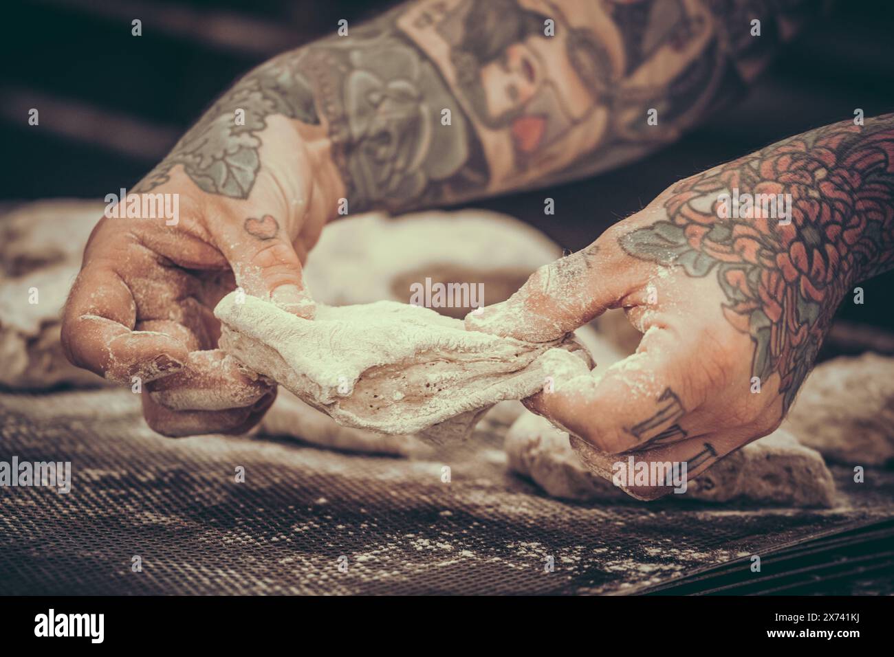A baker with tattoos kneads bread dough in the bakery. Vintage style ...