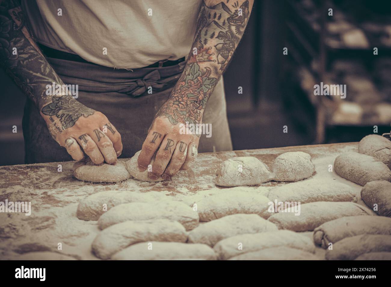A baker with tattoos forms raw dough buns in the bakery, vintage style ...