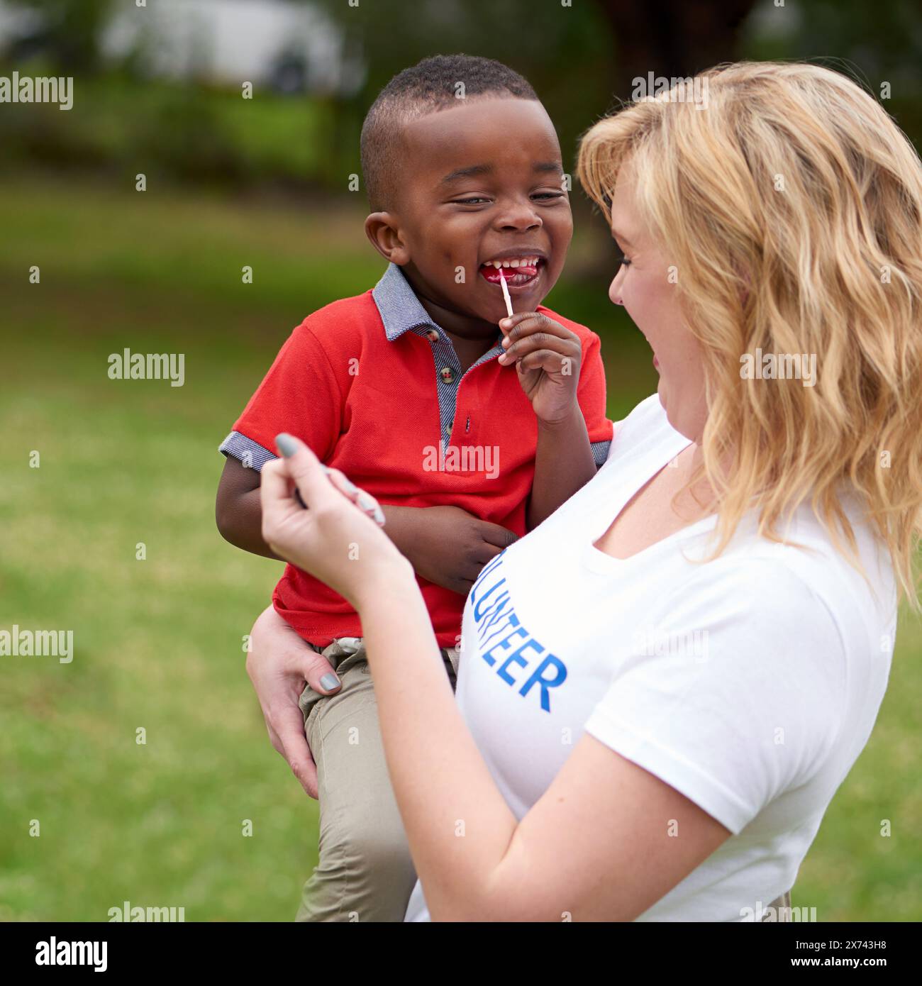 Woman, child and lollipop with smile and volunteer at charity for kids ...