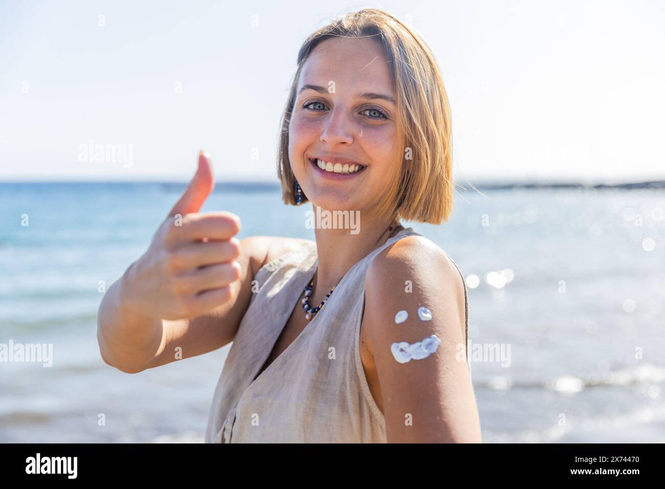 A woman with a smile of suncream on her arm is giving a thumbs up ...