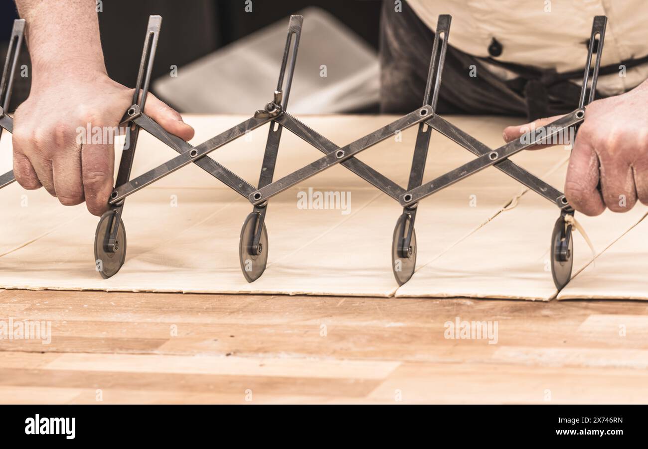 Professional baker cuts dough with multiple wheel pastry cutter ...