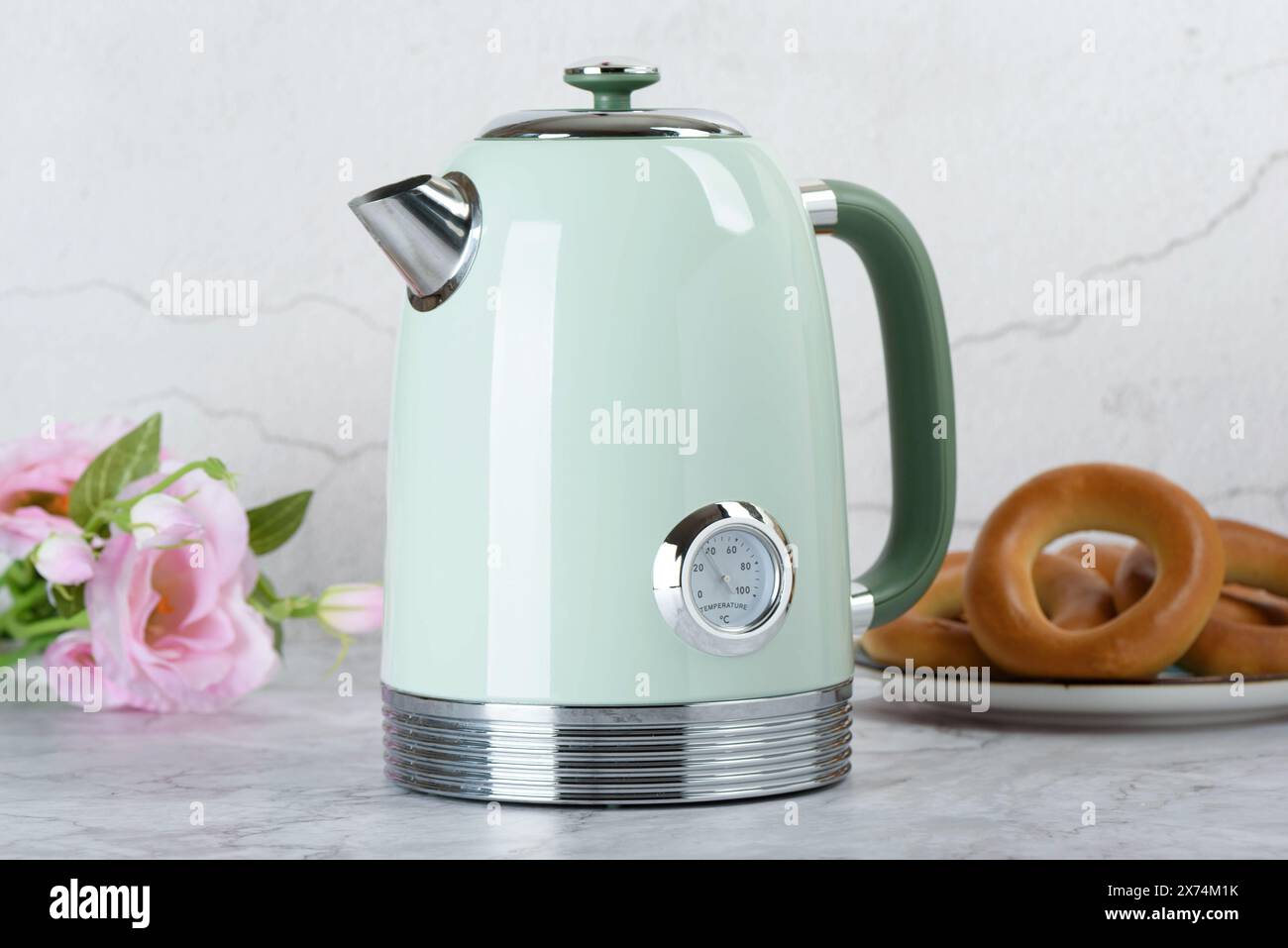 Modern electric kettle on kitchen table with roses and bagels in ...
