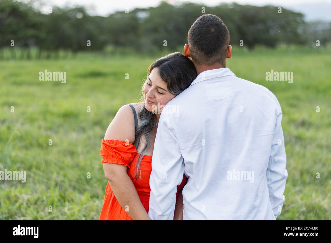 young latina woman smiling and hugging her boyfriend while leaning on his shoulder. man with his ...