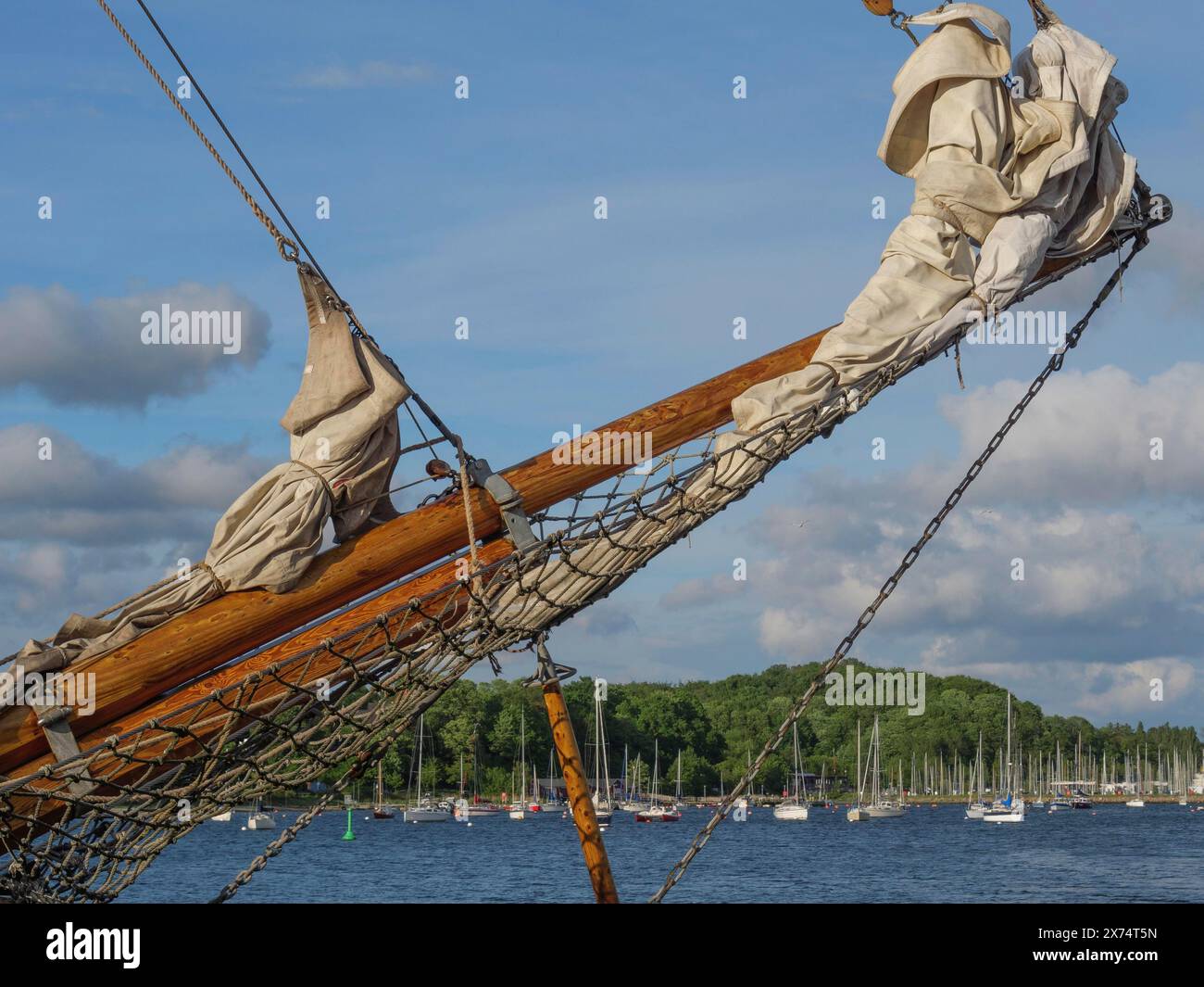 A wooden ship's bow with sail and rig in the foreground, colourful ...