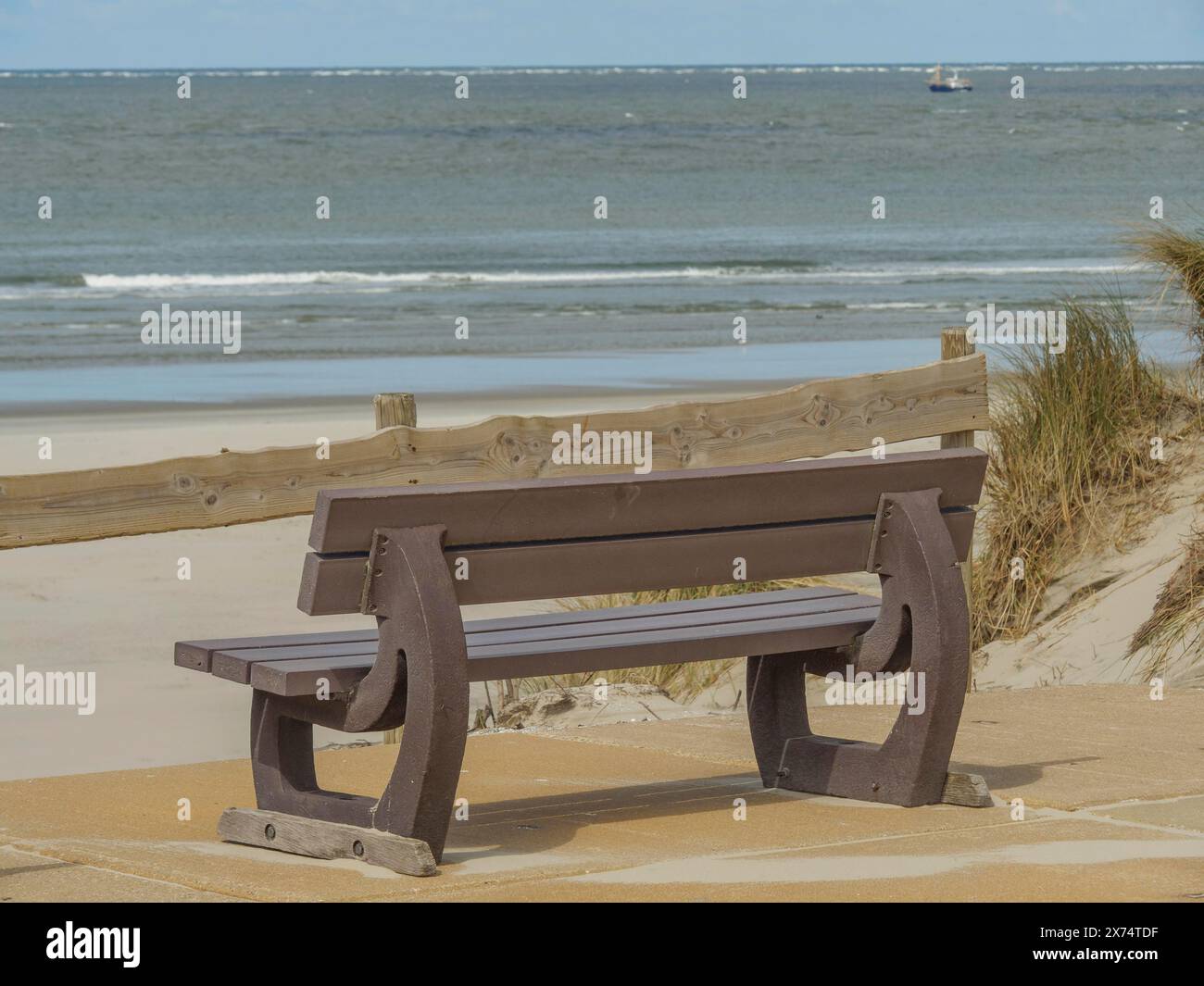 Wooden bench with a view of the sea, with dune grass and a wooden fence ...