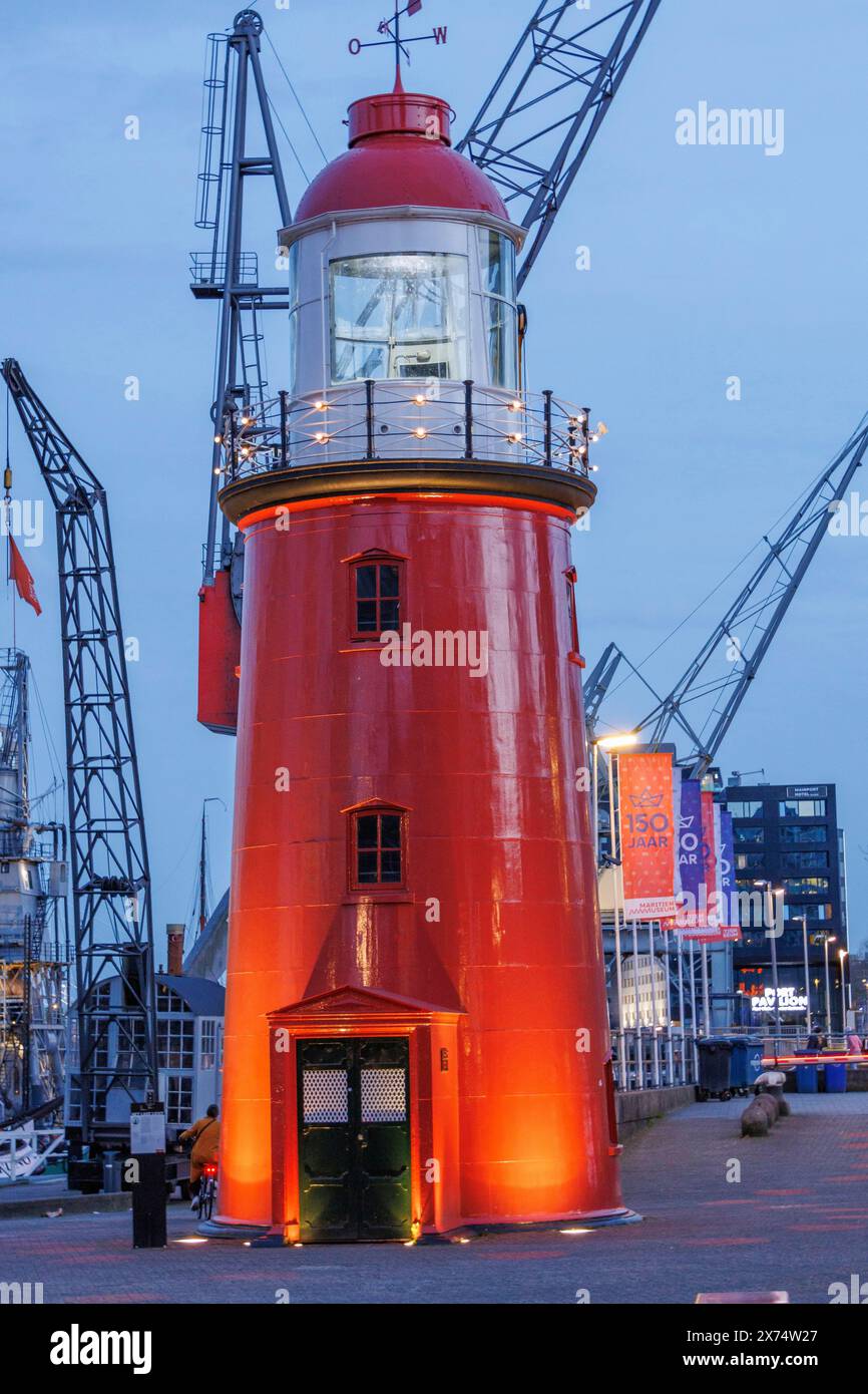 A striking red lighthouse illuminated at night, surrounded by harbour ...