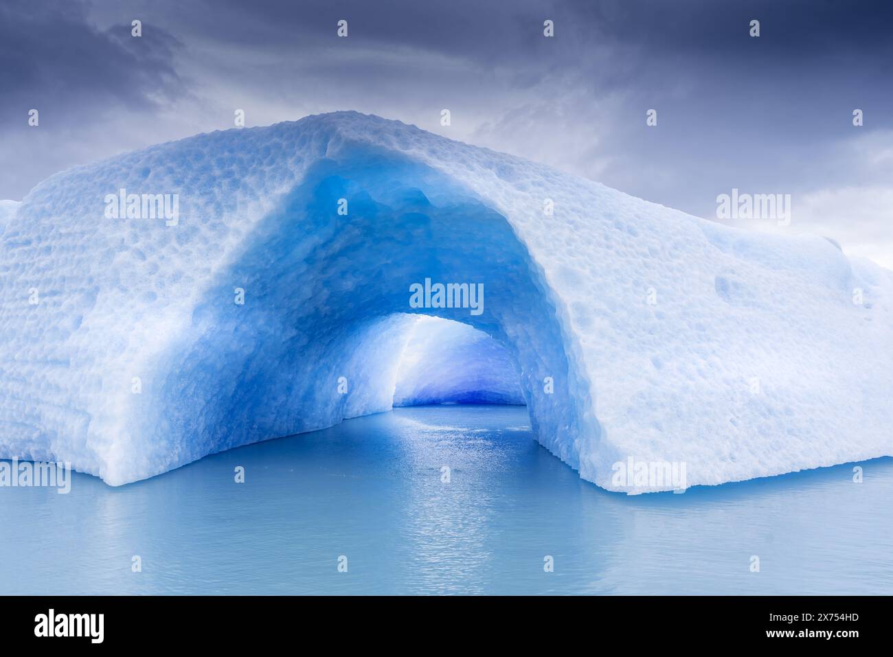 A large blue iceberg cave with a small opening in the middle floating ...