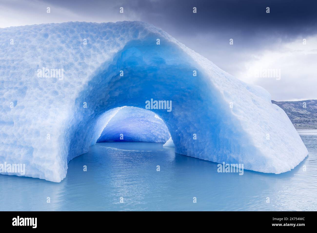 A large blue iceberg block with a hole in it floating on Argentino Lake ...