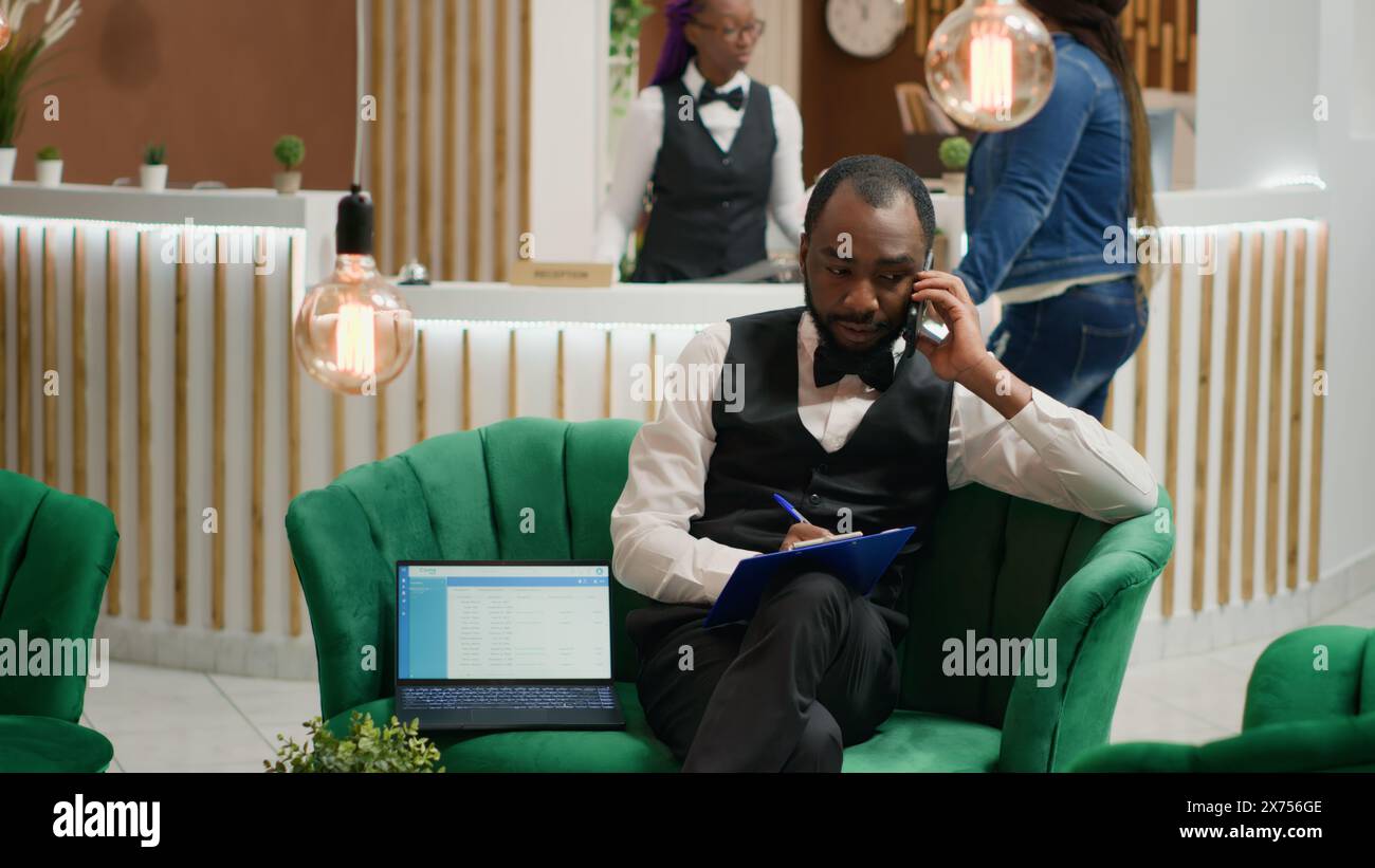 Bellboy talking on phone and taking notes, sitting in lobby at five ...