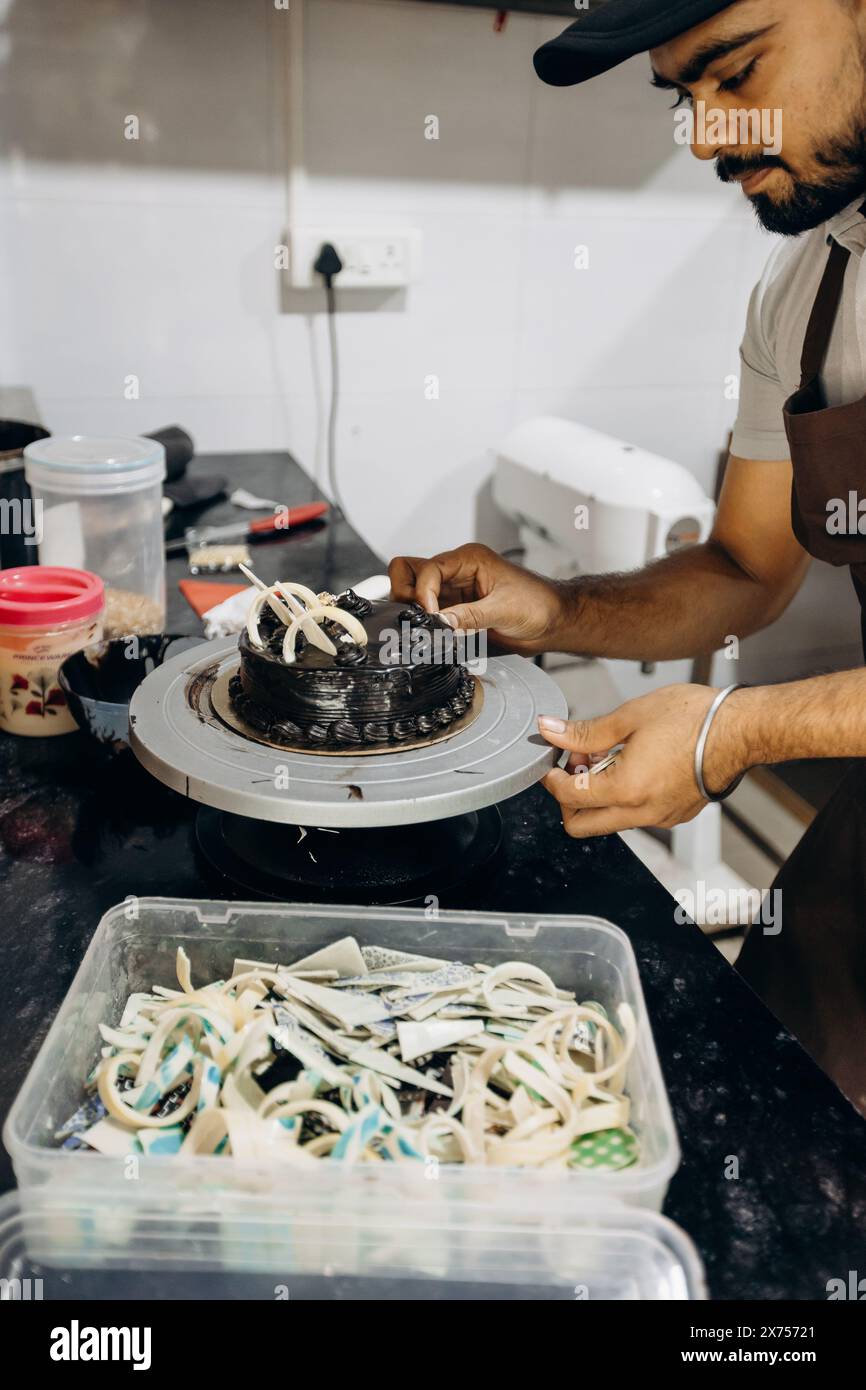 Attractive Indian male chef decorates candied chocolate cake in his ...