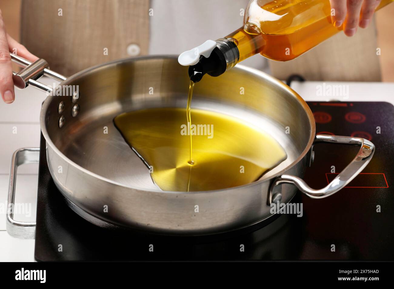 Vegetable fats. Woman pouring cooking oil into frying pan on stove ...