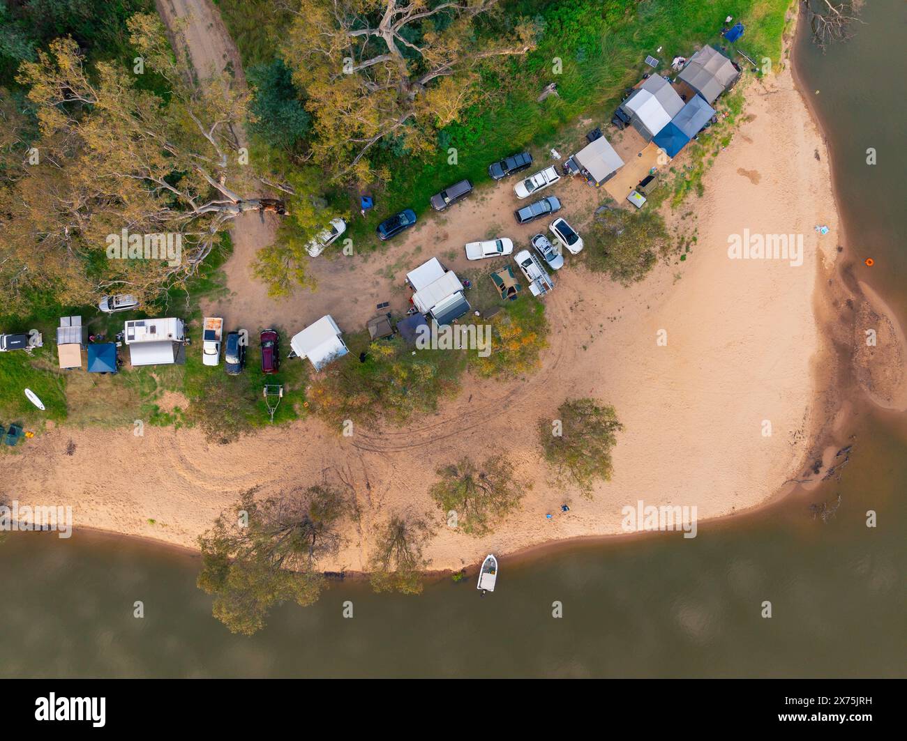 Aerial view of a line of caravans and tents camping on a sandy shore of ...