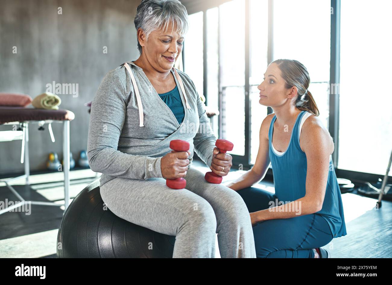 Fitness, personal trainer and senior woman with dumbbell in gym for physiotherapy, support or ...