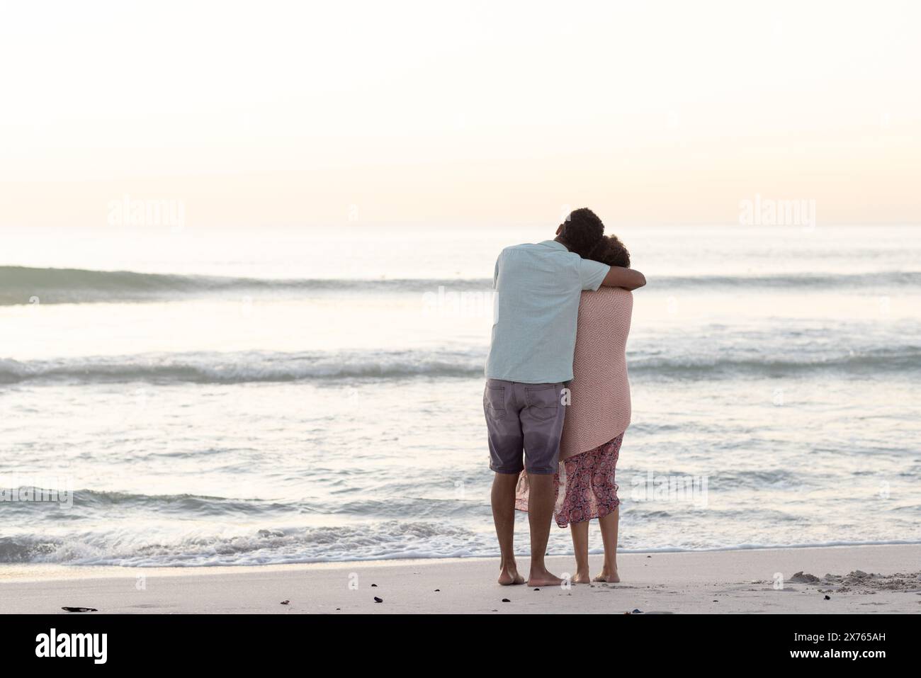 At beach, diverse couple embracing, watching ocean waves Stock Photo ...