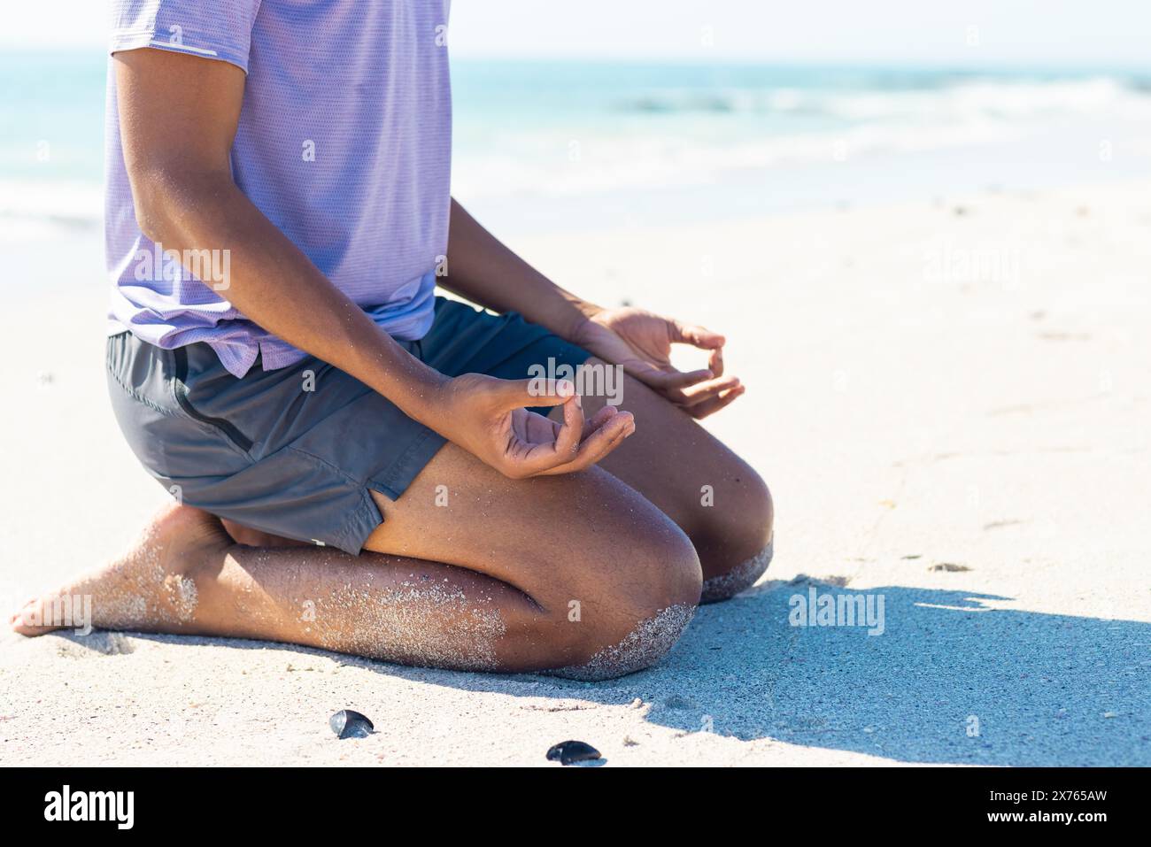 At beach, biracial young man meditating, waves in blue background Stock ...