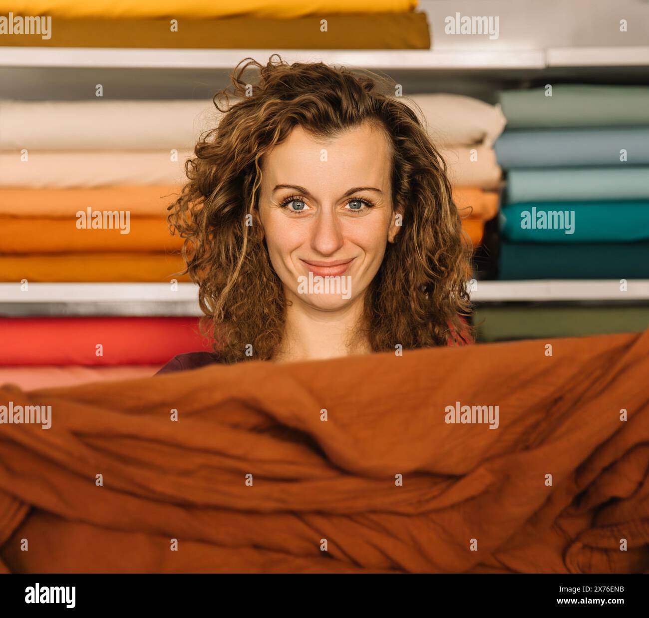 A joyful fashion designer playfully peeks over a large swath of fabric ...