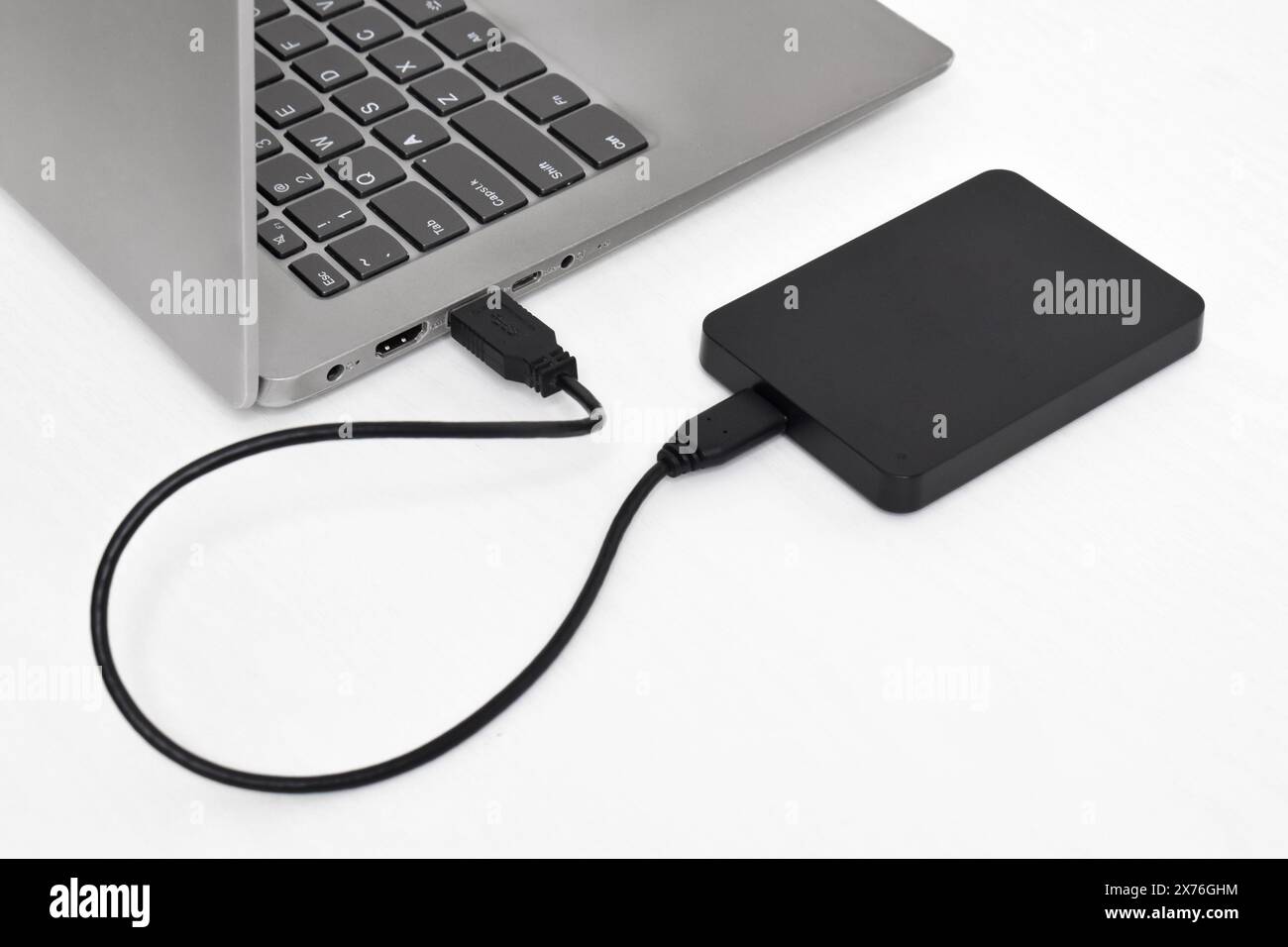 External backup hard disk drive connected to laptop on white background ...