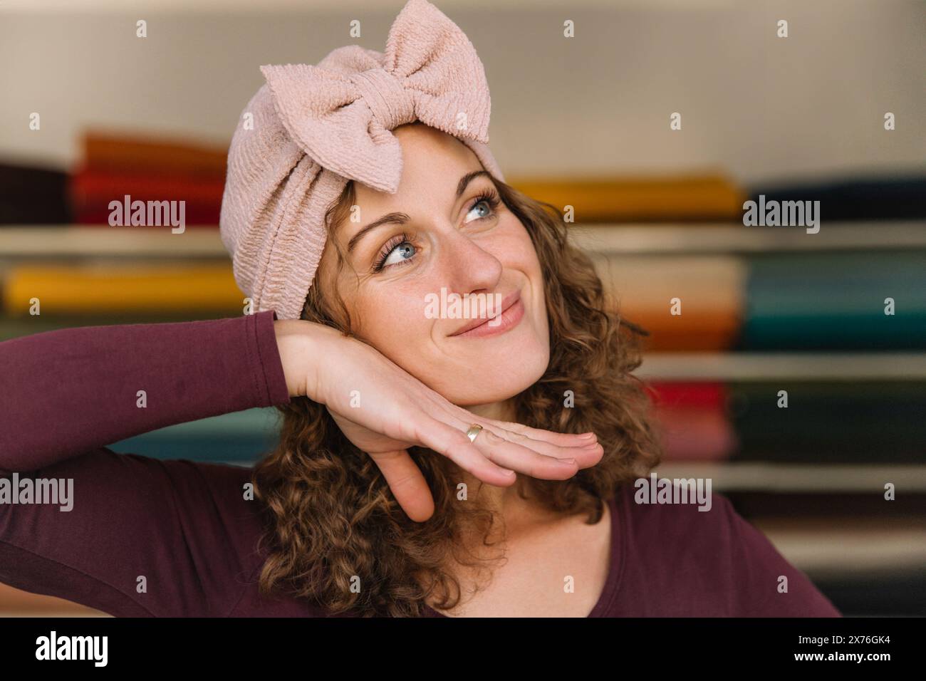 A thoughtful fashion designer poses in her studio, resting her chin on ...