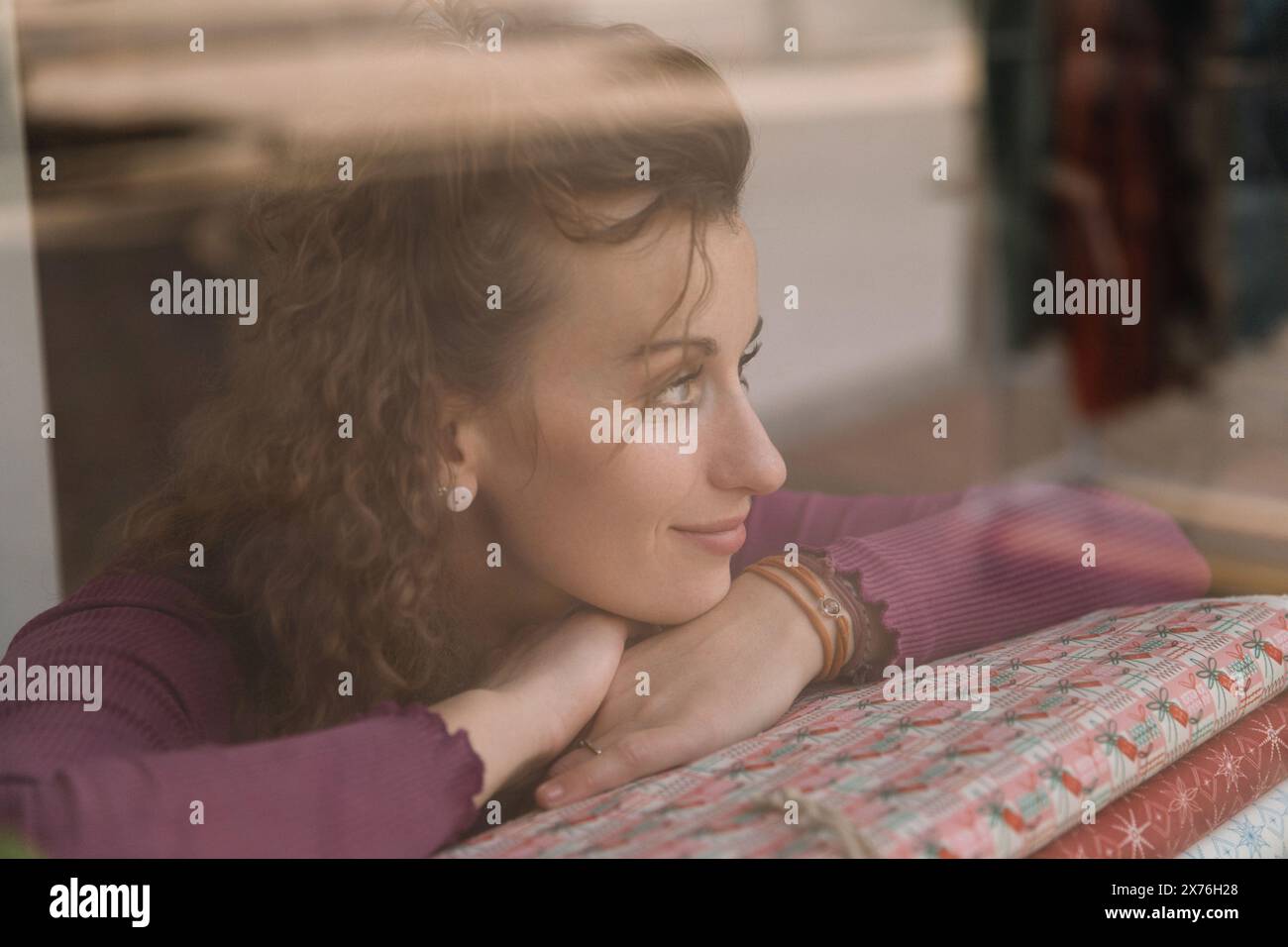 Woman with curly hair resting her chin on her hands, looking outside ...