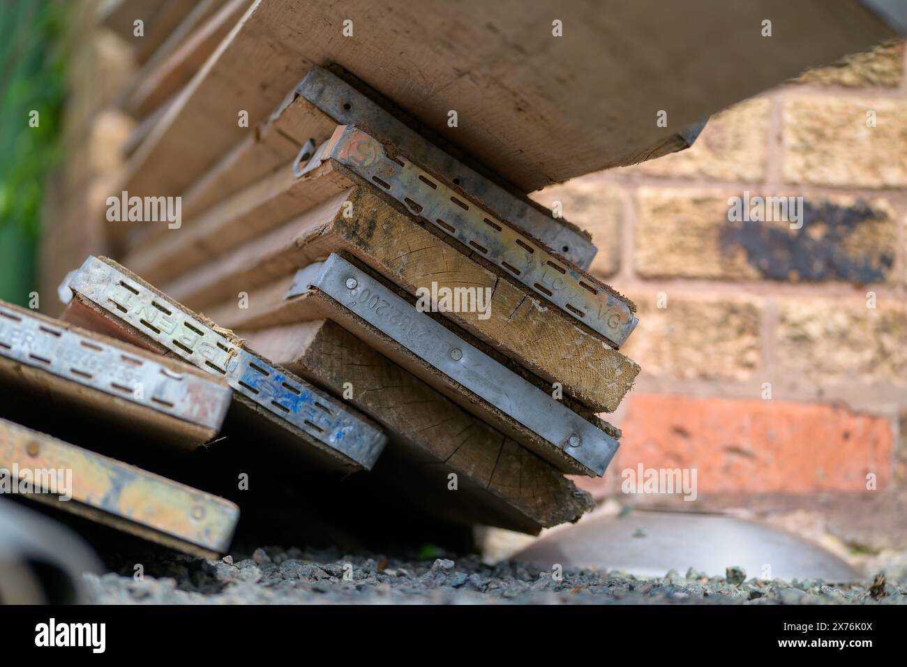 A pile of scaffolding boards leaning against the side of a brick ...